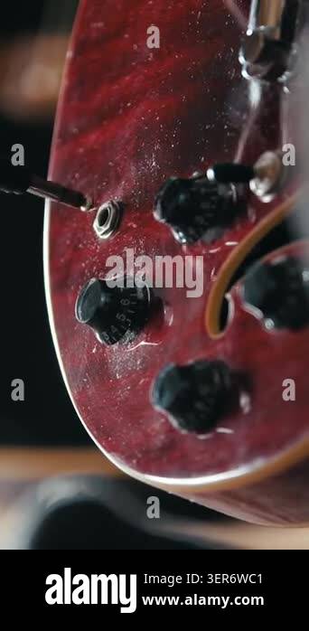 Male guitarist hand plugging a jack cable into a dusty red semi-hollow ...