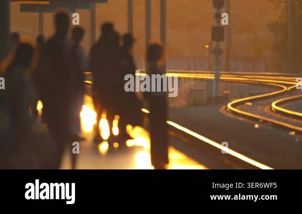 Groups of people stand at a train station during sunset. Shadows ...