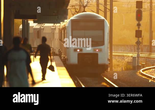 A train pulls into the station as sunlight shines through the evening ...