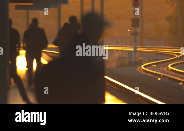 Shadows of people stand at a train station as the sun sets. The warm ...