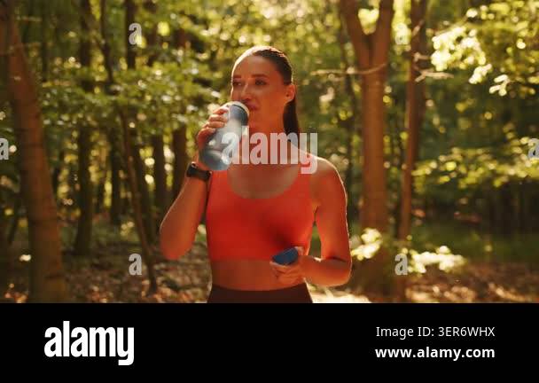 Lady drinking water after workout in forest, enjoying her time outdoors ...
