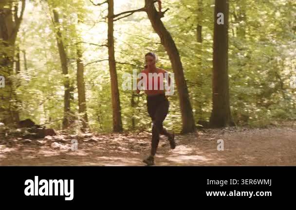 Woman running on path in forest surrounded by trees, listening music in ...