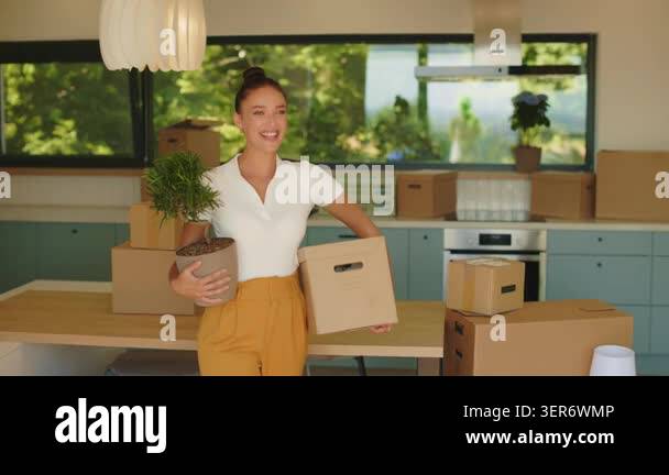 Smiling young woman walking with cardboard box and houseplant in her ...