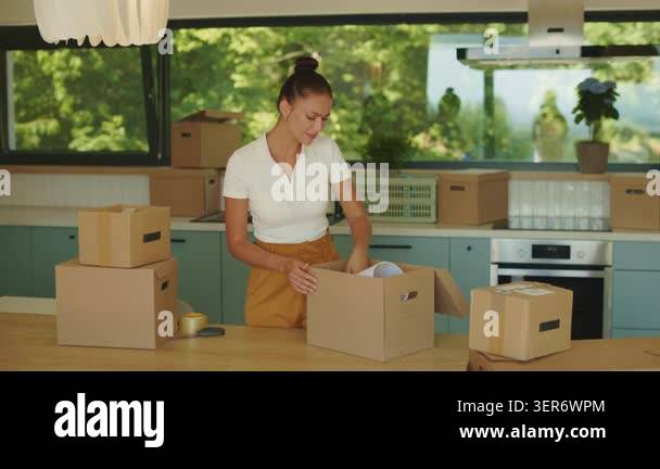 Young woman unpacking belongings from cardboard boxes at modern kitchen ...