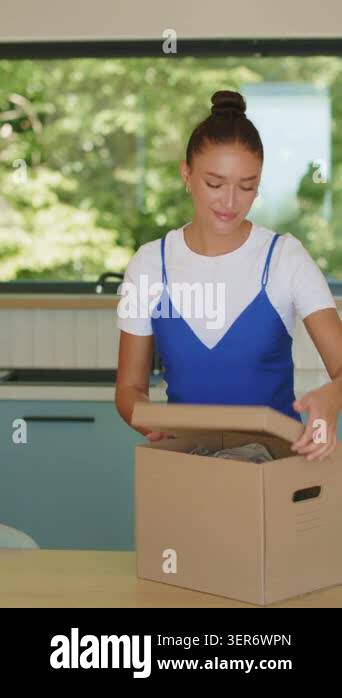 Vertical footage of young woman unpacking personal items from cardboard ...