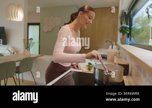 Woman stirring food in saucepan with wooden spoon, carefully checking ...