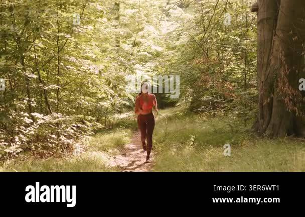 Fit woman running up path in the forest, being focused on workout ...