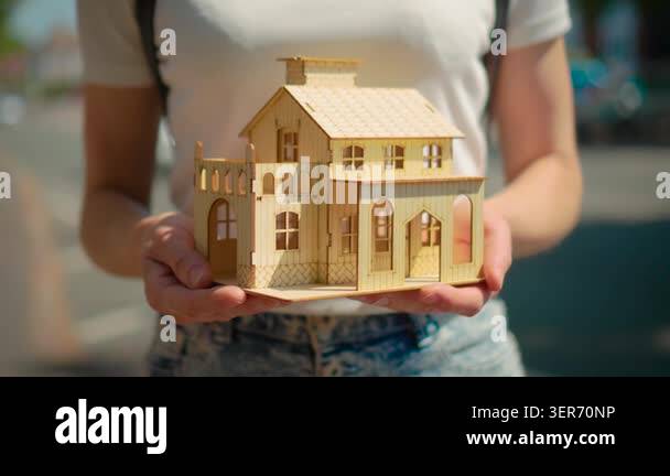 Female hands presenting tiny cottage model on city street. Housing loan ...