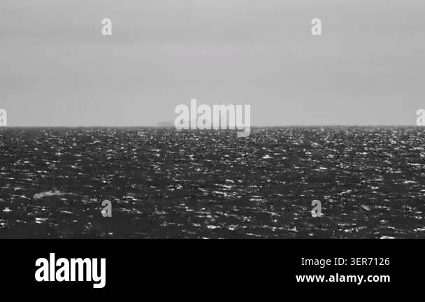 A person stands by the ocean looking towards a distant land. The water ...