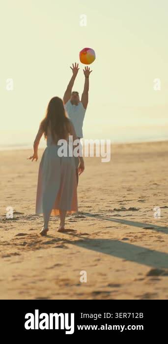 A couple enjoys the beach as they toss a colorful ball back and forth ...