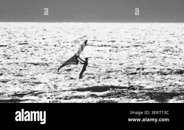 A person is windsurfing at the beach. They are riding on the waves and ...