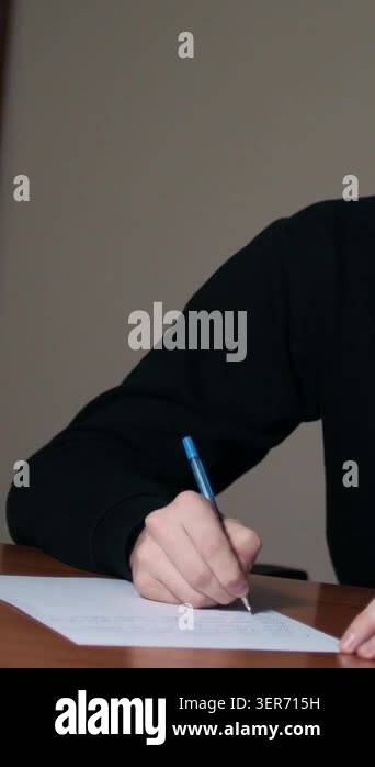 A black hair man in dark room writes text by pen on paper, close up ...