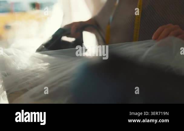 Womans hands ironing white delicate tulle fabric with hot steam in a ...
