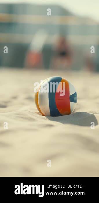 A volleyball sits on the sand at a beach. Players are enjoying a game ...
