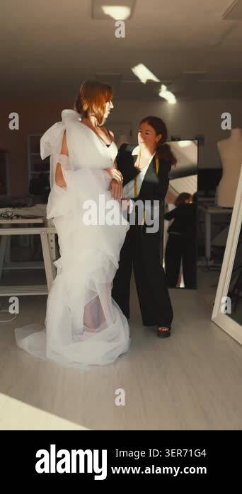 Female couturier working on a custom white gown with a client in a ...