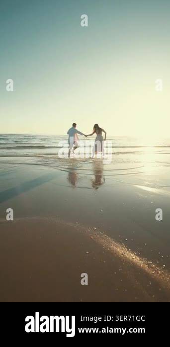 A couple runs together on the beach as the sun sets over the ocean ...