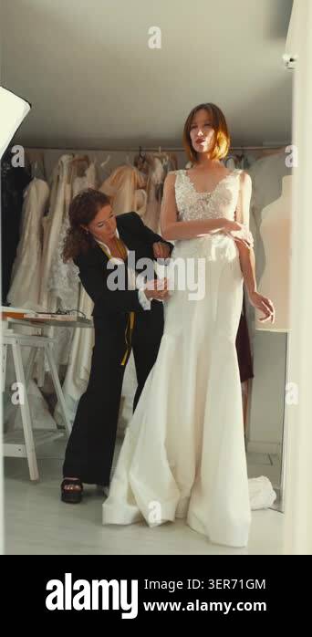 Professional tailor fitting an elegant white wedding dress on a young ...
