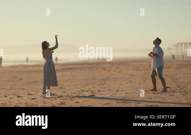 A couple stands on the beach playing with a colorful beach ball as the ...