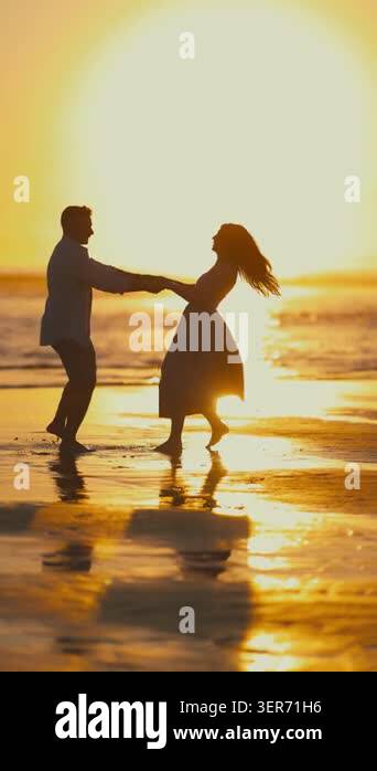 A couple enjoys a moment together while dancing on the beach. The sun ...