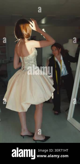 Young woman trying on a custom-made formal dress with the help of a ...