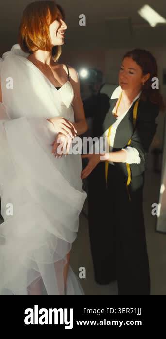 Fashion designer fitting a beautiful bride with her custom-made wedding ...