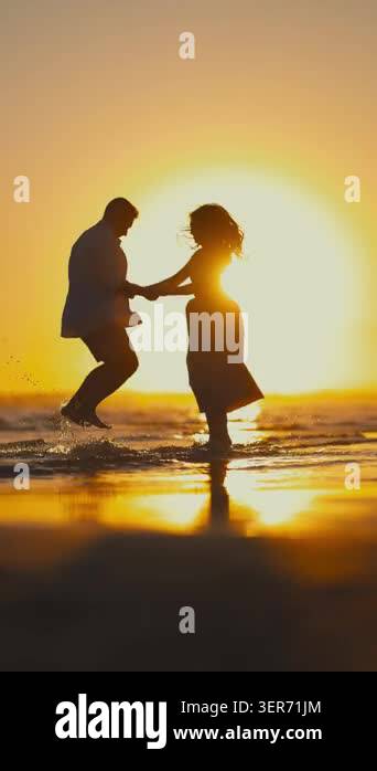 A couple stands in shallow water at the beach during sunset. The sun is ...