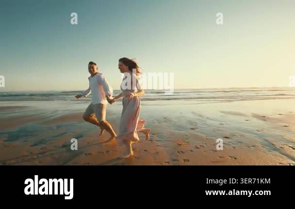 A couple enjoys time on the beach as they run together. The sun sets ...
