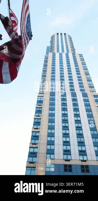 Flags of the United States wave in the wind near a tall building. The ...