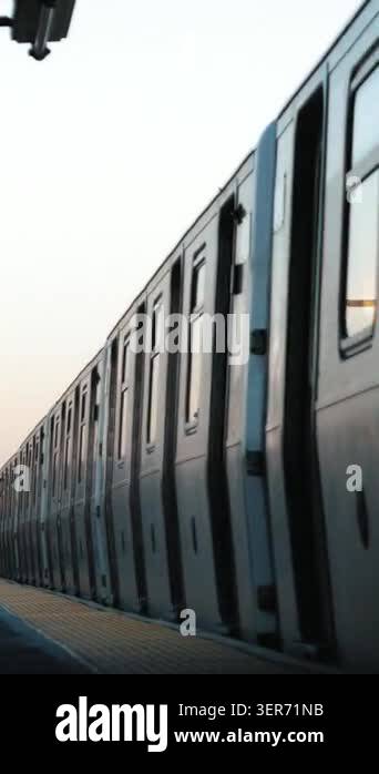 A subway train approaches the station at sunset. People wait on the ...