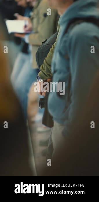 Many people stand in line at a station with bags and notebooks. Some ...