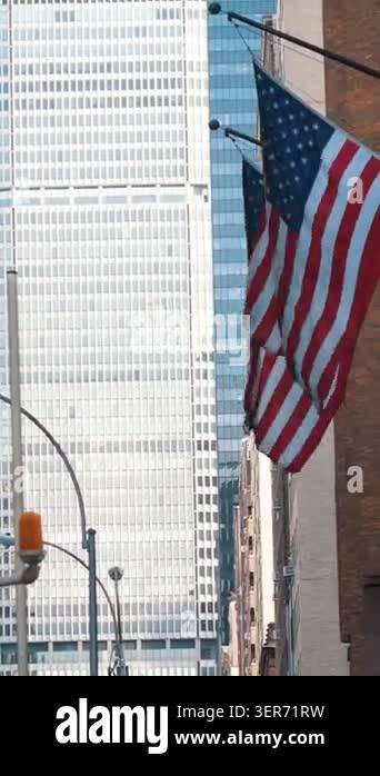 American flags flutter on a busy city street. Tall buildings reflect ...