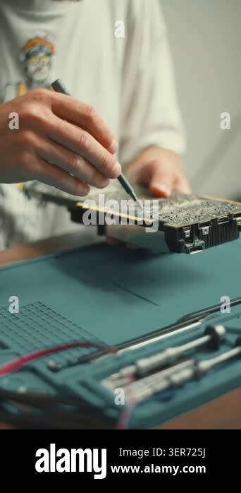 A person is working on a computer part with a pen and tools on a table ...