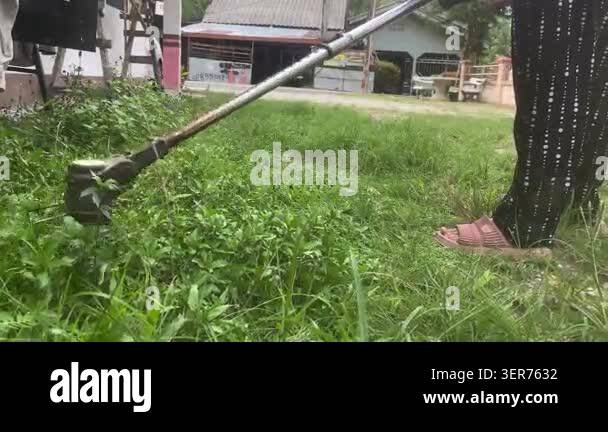 Close-up of a person using a grass trimmer to cut overgrown lawn in a ...