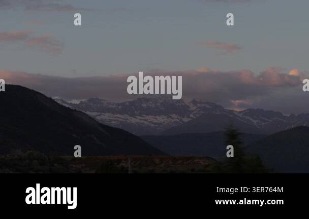 Snowy peaks beyond blurred branches at dusk evoke moody travel and ...