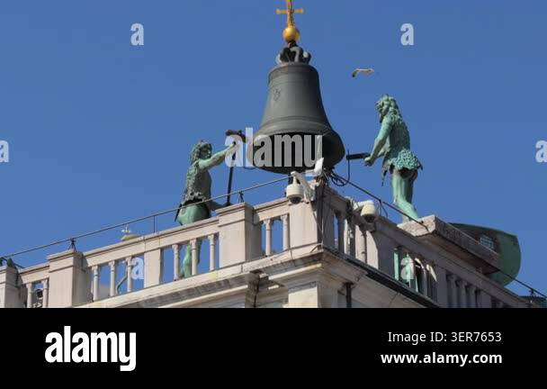 A large church bell swings between bronze figures as a seagull flies by ...