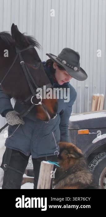 Woman in cowboy hat with horse and dog standing on snow field ...