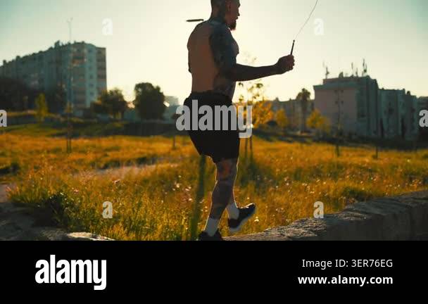 A man skips rope in an open field near tall buildings. He enjoys his ...