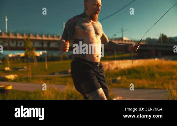 A man is skipping rope in a park at sunset. He is wearing shorts and is ...
