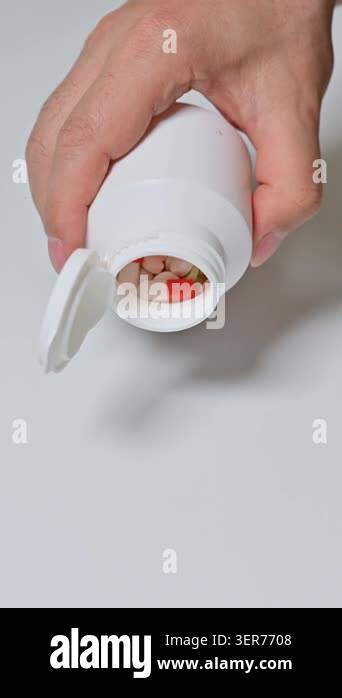 Medical pills and capsules falling out of a white bottle held by a hand ...