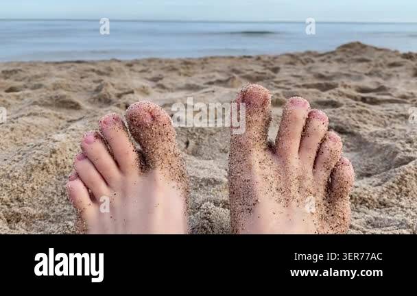 Close-up video of feet covered with sand on a beach with the sea in the ...