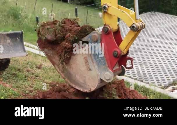 Mini excavator bucket filled with fresh soil lifting over green grass ...