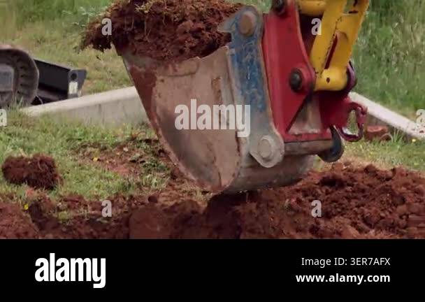 Close up of a mini excavator bucket lowered into a deep pit for digging ...
