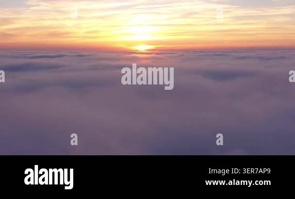 Aerial flight above glowing clouds at sunset with golden sunlight ...