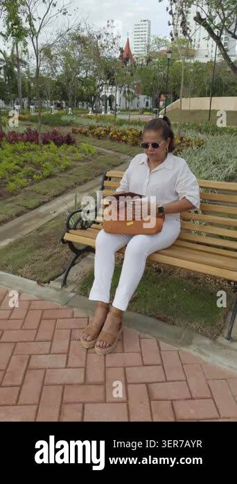 Stylish mature woman sitting on a wooden bench in a city park while ...