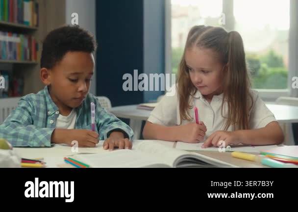 Two multiethnic little kids wring in textbook studying communicating ...