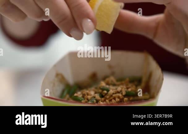 Person adds fresh lemon juice to a bowl of Asian food with and peanuts ...