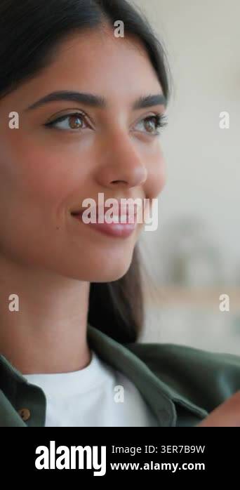 Pensive smiling Arabian Indian woman using smartphone at home indoors ...