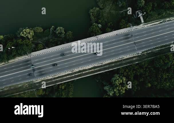 Cars move along the road next to a river while trees line the banks and ...