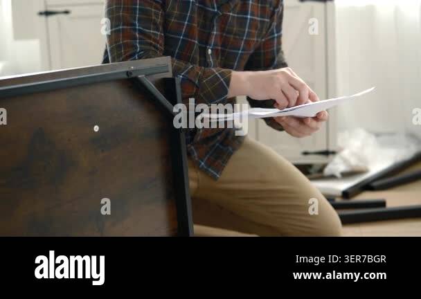 Man follows instruction manual while putting together furniture at home ...