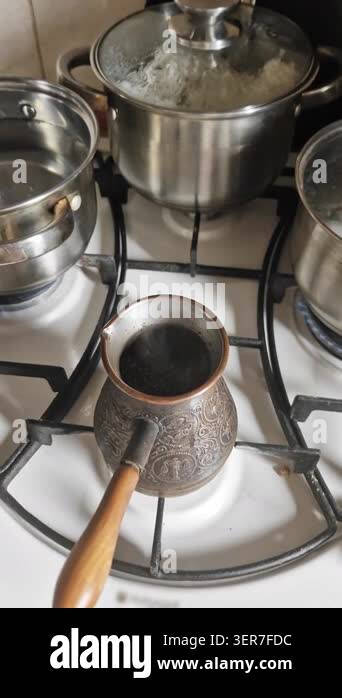 An ornate copper cezve filled with dark coffee sits on a white gas ...